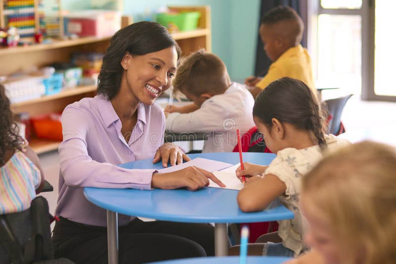 Female Primary or Elementary School Teacher Helping Students at Desks ...