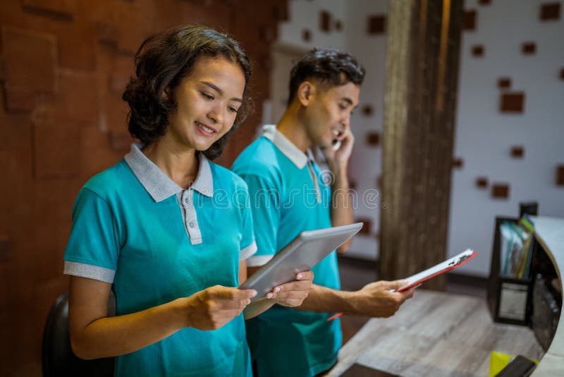 Female Receptionist Using Tablet with Male Receptionist Working Stock ...