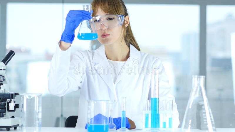 Female Research Scientist Looking at Blue Solution in Flask in ...