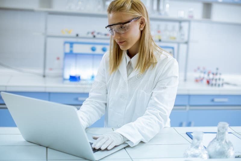 Female Researcher in White Lab Coat and Protective Goggles Using Laptop ...