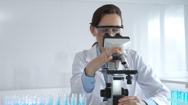 Female Scientist in Lab Coat and Safety Glasses Using Microscope ...