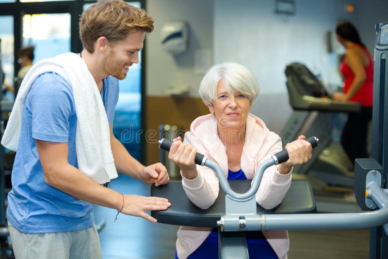 Female Senior in Gym Assisted by Trainer Stock Photo - Image of success ...