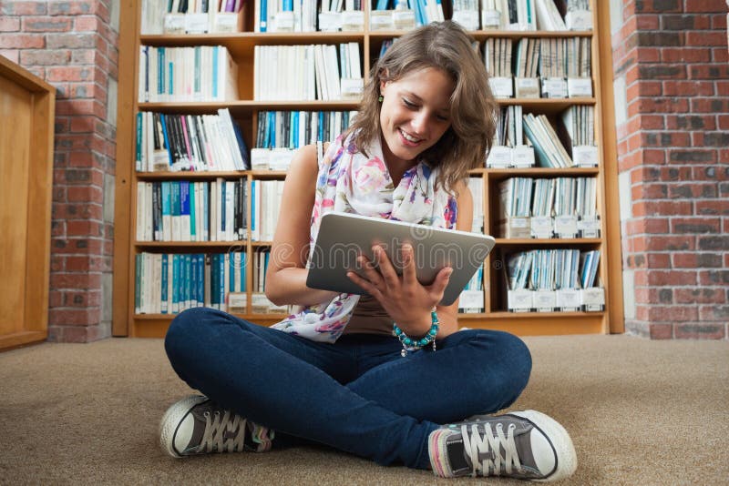 Female Student Against Bookshelf Using Tablet PC on the Library Floor ...