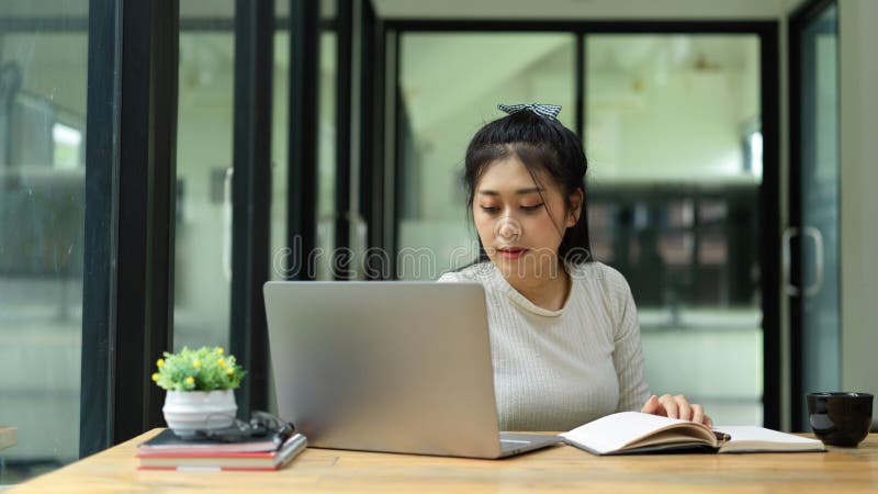Female Student Reading Book and Doing Homework with Laptop in Study ...