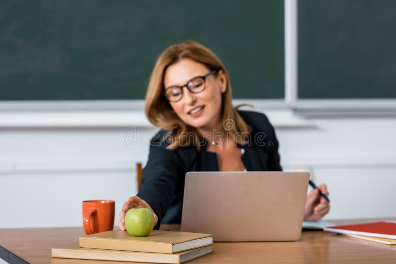 Female Teacher Sitting at Computer Desk and Reaching for Apple Stock ...