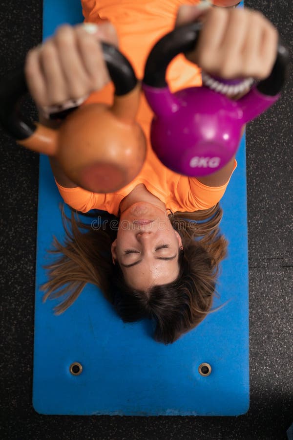 A Female Trainee Lifting a Pair of Kettlebells during a Workout Session ...