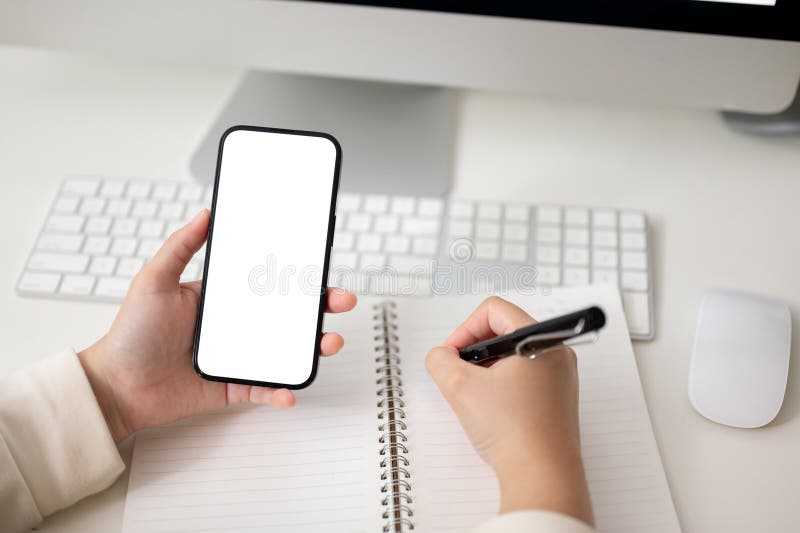 A Female Using Her Smartphone and Taking Notes on Her Notebook at Her ...