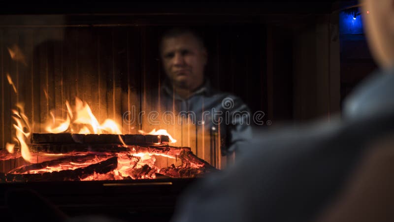 Fire is Burning in the Fireplace, a Man is Looking at Him. Reflection ...