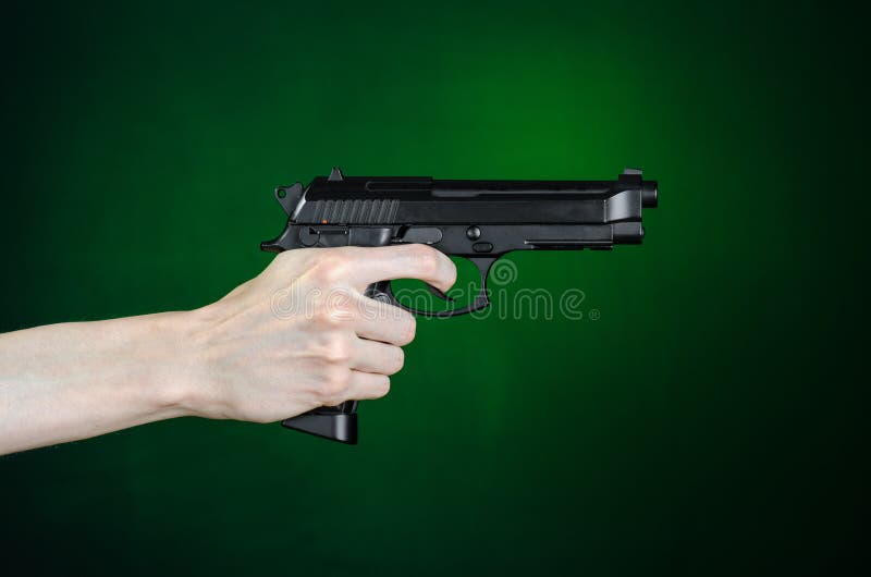 Firearms and Murderer Topic: Human Hand Holding a Gun on a Dark Green ...