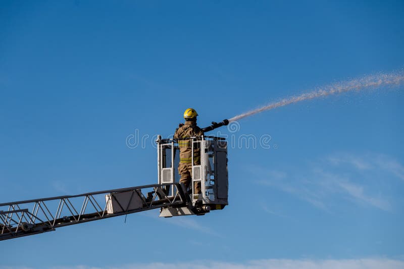 A Firefighter is Spraying Water from a Hose while Standing on a Ladder ...