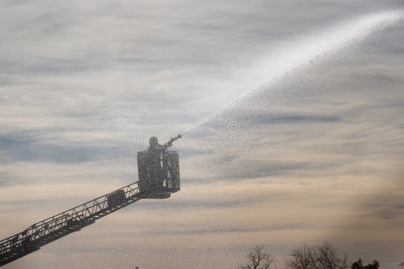 A Firefighter is Spraying Water from a Hose while Standing on a Ladder ...