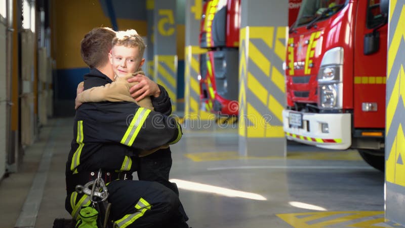 Firefighter in Uniform Hugs a Little Boy Near a Fire Engine at Station ...