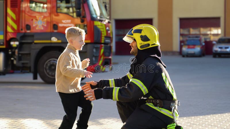 Firefighter in Uniform Hugs a Little Boy Near a Fire Engine at Station ...