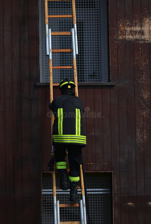 Firefighter in a Uniform and Protective Helmet Climbing a Ladder ...