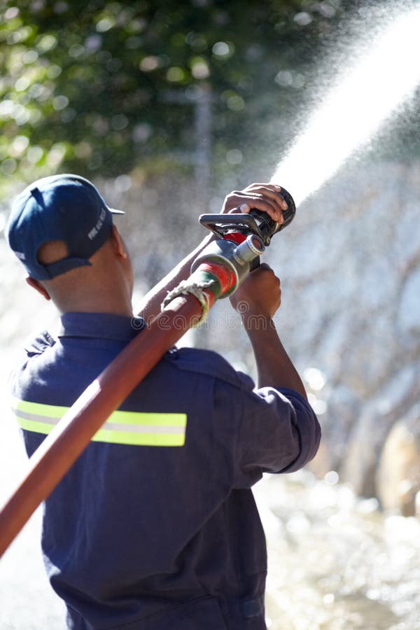 Fireman at Work. Rearview Shot of a Fireman Spraying Water with a Fire ...