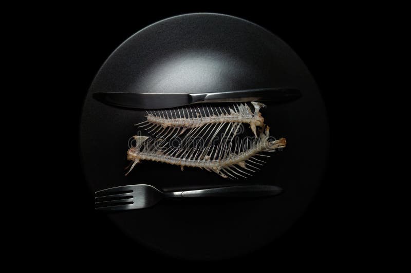 Two Fish Spines on a Black Plate with a Fork and a Spoon Stock Photo ...