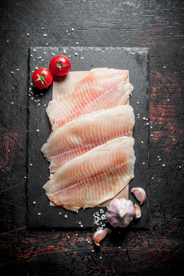 Fish Fillet on Paper on a Stone Board with Garlic and Tomatoes Stock ...