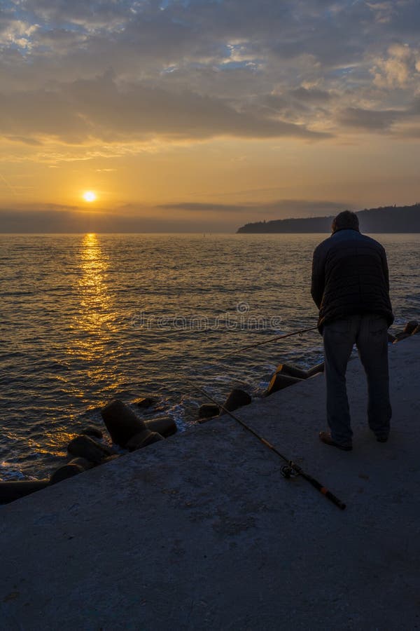 A Fisherman Catching Fish at Sunrise at a Seaport. Stock Photo - Image ...