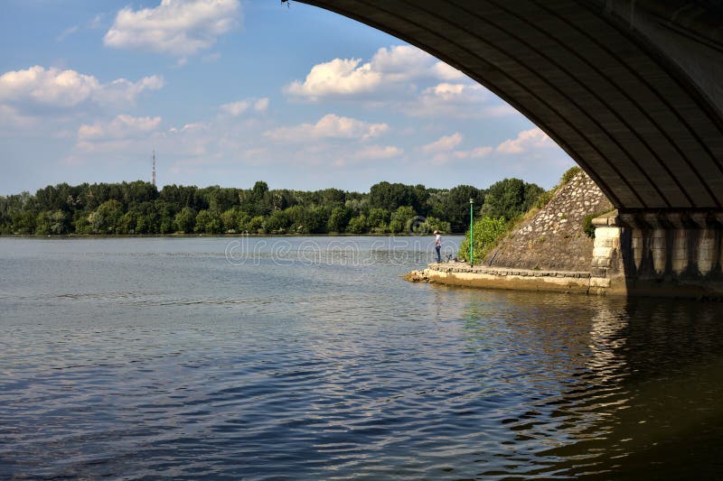 Fisherman on the Shore of a Lake Under a Bridge on a Sunny Day in ...