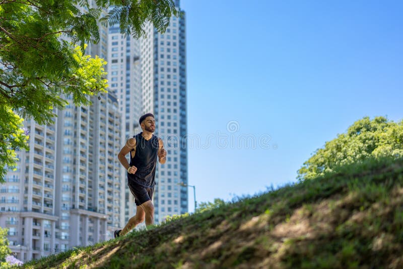 Fit Young Man Enjoying a Dynamic Run through a Hilly Park Setting with ...