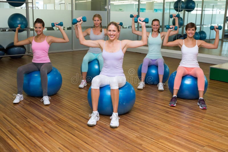 Fitness Class Holding Dumbbells on Exercise Balls in Studio Stock Photo ...