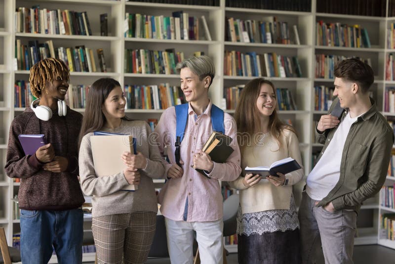 Five Multi Ethnic Schoolmates Standing in Library and Talking Stock ...