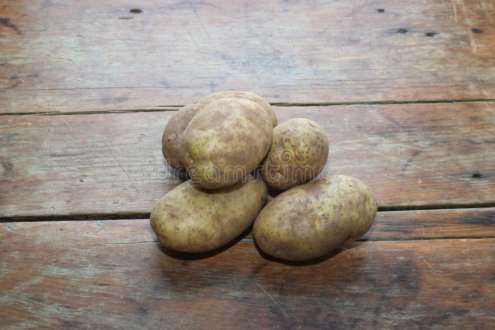 Five Potatoes on a Distressed Wooden Table Stock Photo - Image of ...