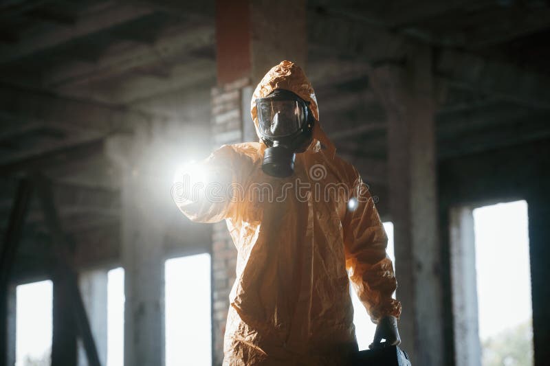 With Flashlight. Man Dressed in Chemical Protection Suit in the Ruins ...
