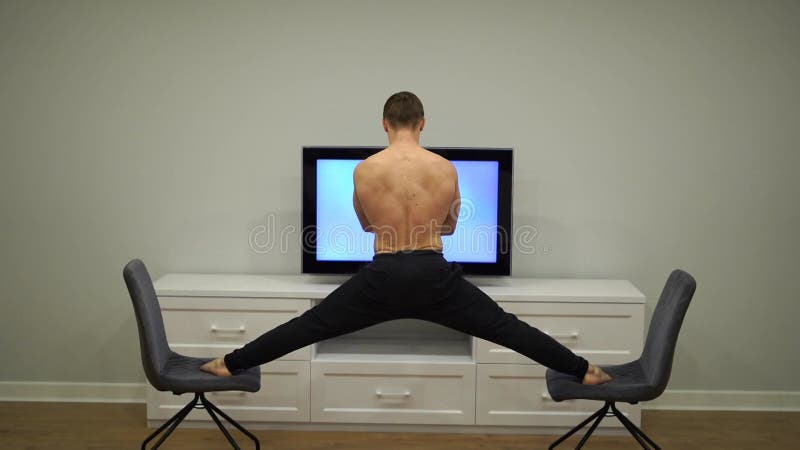Flexible Man Keep Balance in Split between Two Chairs Watching TV ...