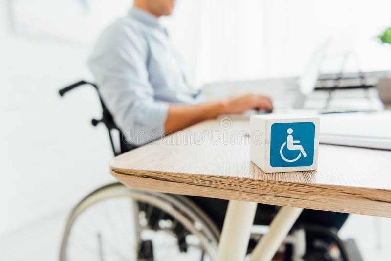 Focus of Cube with Disabled Sign and Man in Wheelchair Sitting at Table ...