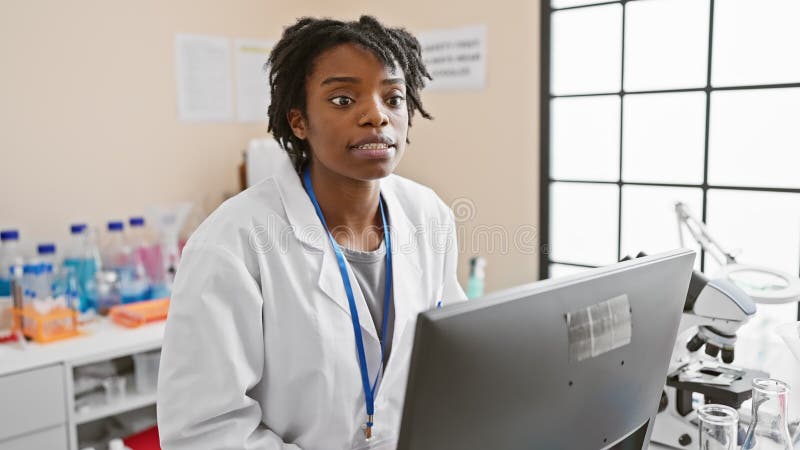 A Focused African American Woman Scientist in a Lab Coat Working in a ...