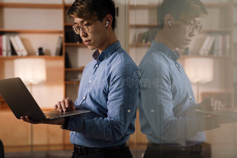 Focused Asian Guy in Earphones Working with Laptop in Office Stock ...