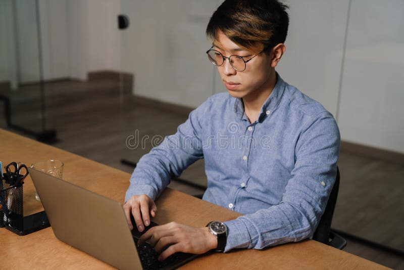 Focused Asian Guy Working with Laptop while Sitting at Table in Office ...
