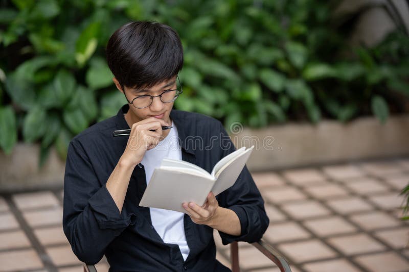 A Focused Asian Man is Reading a Book and Working on His Assignment at ...