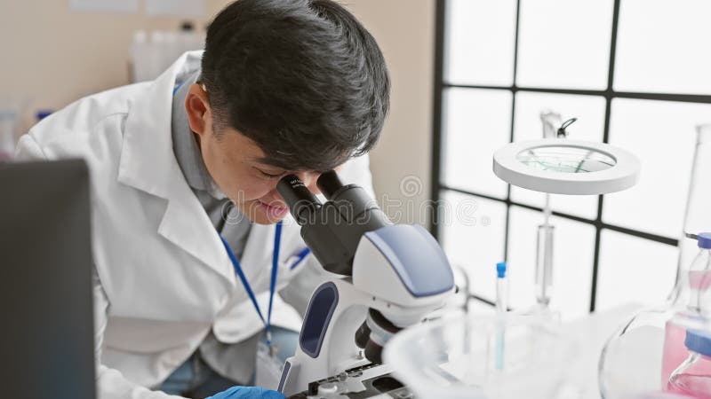 A Focused Asian Man Using a Microscope in a Modern Laboratory Setting ...
