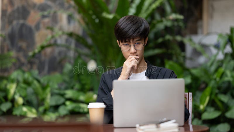 A Focused Asian Man Working on His Laptop Computer, Working Remotely at ...