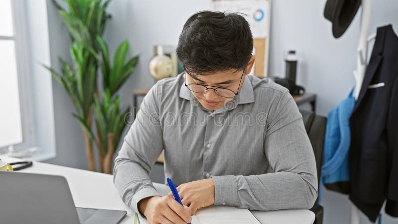 A Focused Asian Man Writing in an Office Setting, Embodying ...