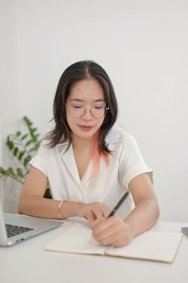 A Focused Asian Woman is Working Remotely from a Cafe, Taking Notes or ...