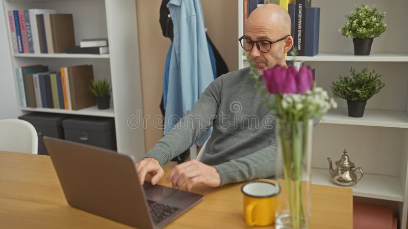 A Focused Bald Man with a Beard Using a Laptop at a Home Office with ...