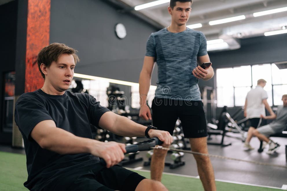 Focused Beginner Sportsman with Personal Instructor Working Out in Gym ...