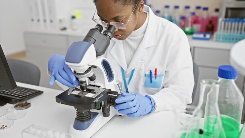 A Focused Black Woman Scientist Operates a Microscope in a Modern ...