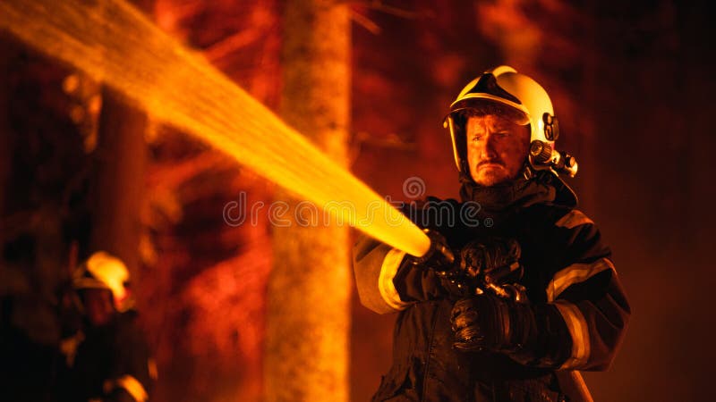 Focused Brave Professional Firefighter Using a Firehose To Fight a ...