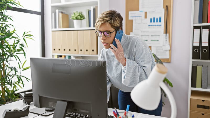 A Focused Businesswoman Talks on a Mobile Phone while Working on a ...
