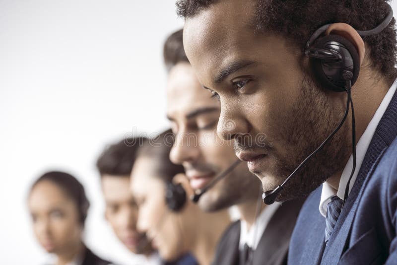 Focused Call Center Operator In Headset Working With Colleagues Behind ...