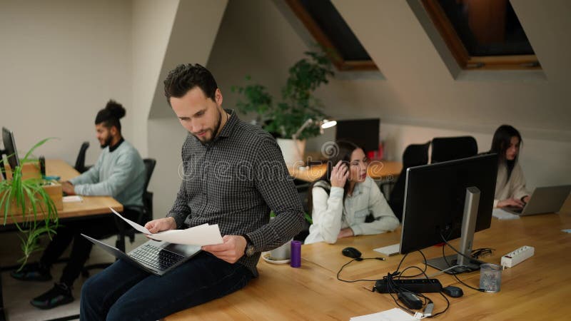Focused Caucasian Young Man Sitting on the Table with Laptop and ... Focused Caucasian Young Man Sitting on the Table with Laptop and ...