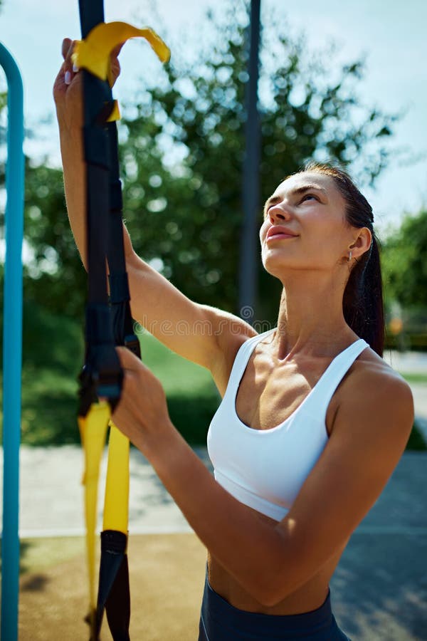 Focused and Determined Woman Adjusts TRX Straps Outdoors, Preparing for ...