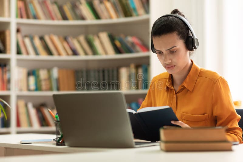 Focused Female Student Reading Book and Using Laptop Computer, Studying ...