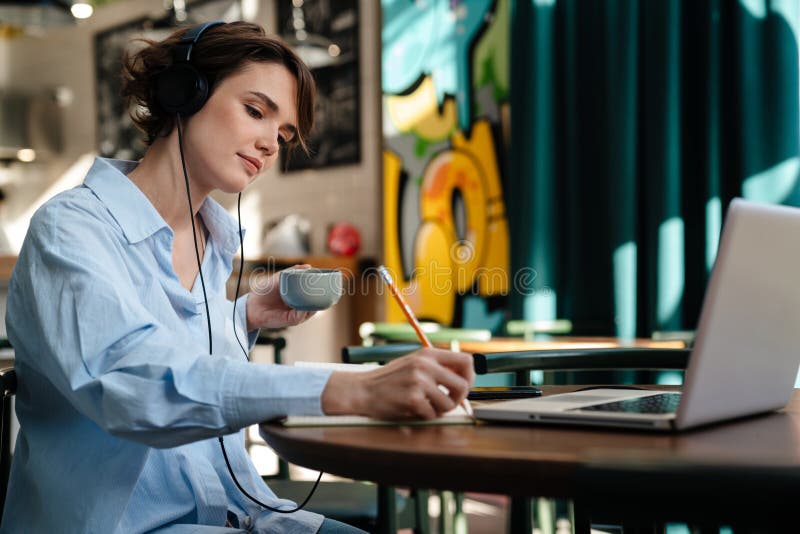 Focused Girl Writing Down Notes while Using Laptop and Headphones Stock ...