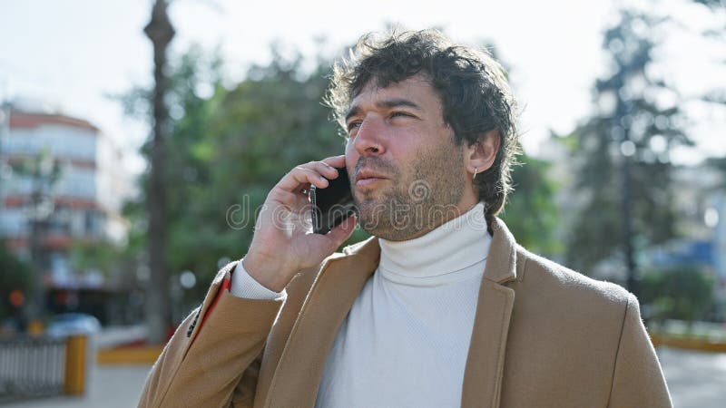 A Focused Hispanic Man with a Beard Talking on a Smartphone in a Sunny ...