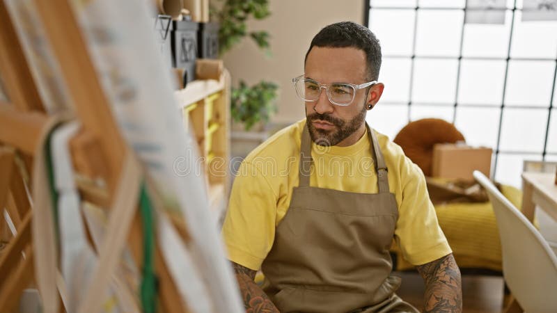 A Focused Hispanic Man with a Beard and Tattoos Wearing Glasses and an ...